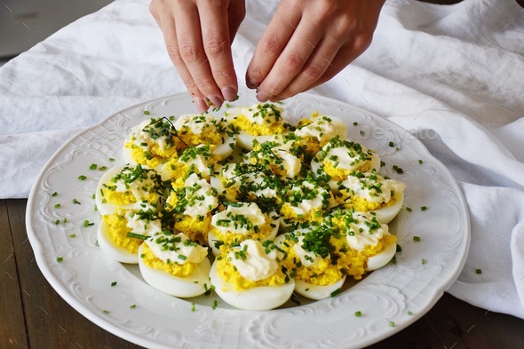 Woman’s hands sprinkle green chives on top of Deviled eggs Stock Photo ...