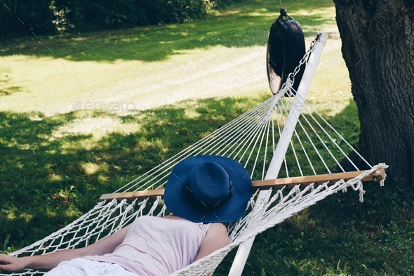 Woman covering her face with a blue hat is laying in a hammock sleeping ...