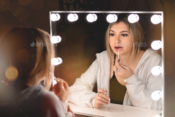 Young teenage girl doing make up in front of vanity mirror with led ...
