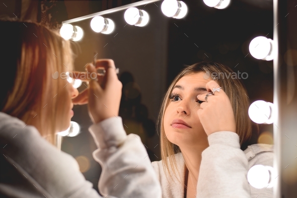 Young teenage girl doing make up in front of vanity mirror with led ...