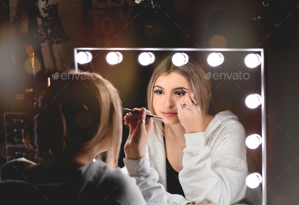 Young teenage girl doing make up in front of vanity mirror with led ...