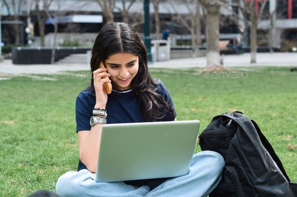 Young girl student sitting on green grass lawn using laptop computer ...