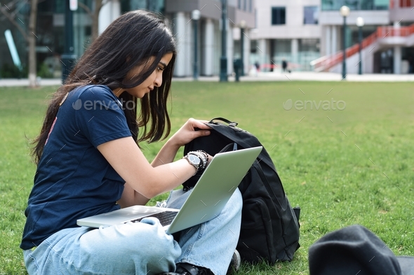 Young girl student sitting on green grass lawn using laptop computer ...