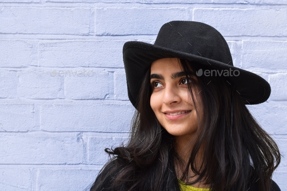 Closeup portrait of young girl in fedora hat standing by violet brick ...