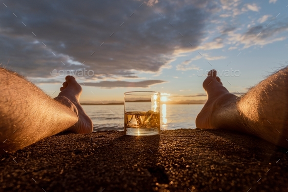 Relaxing with a cocktail alcohol drink between legs in late day sun by ...