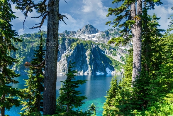Alpine lake with jagged rock mountain peaks framed by evergreen pine ...