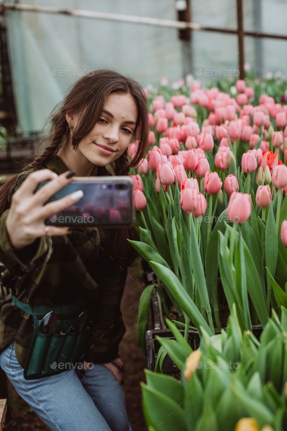 Woman gardener makes selfie. The girl smiles and uses a mobile phone in the tulip flowers ...