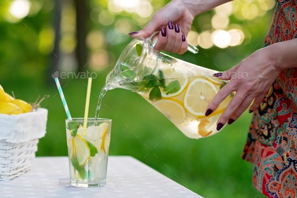 Female hands pour refreshing cold lemonade with lemons in ice and mint ...