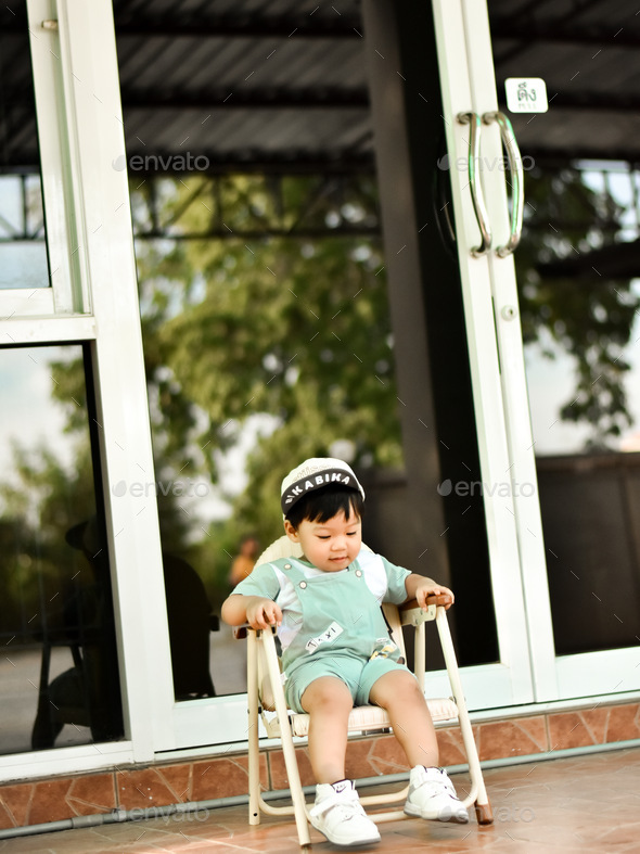 Cute little boy sitting on a chair in the home Stock Photo by Jsttanrak