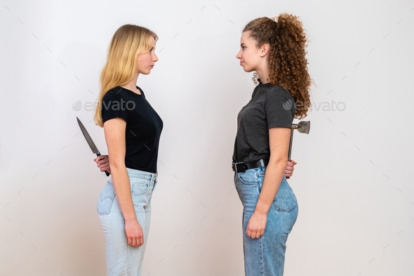 two angry women standing face to face and hiding knife and axe behind ...