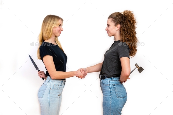 two smiling women standing face to face and hiding knife and axe behind ...