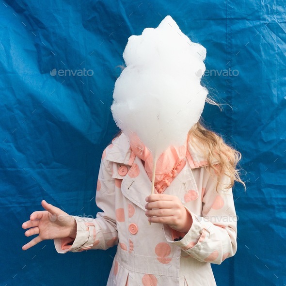 Girl holding big candy floss in the front of face standing over blue ...