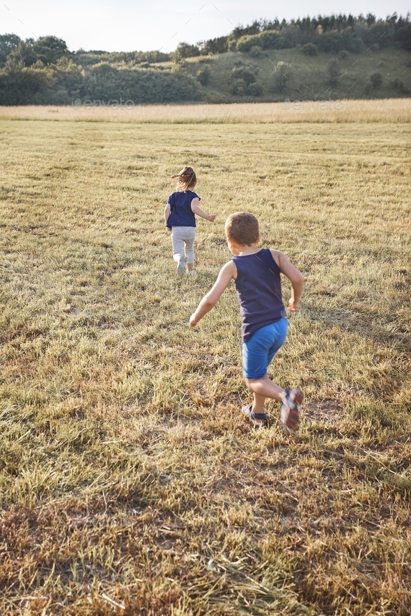 Children running through field. Little girl and boy playing in the ...