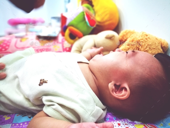 Baby crying while lying down on the bed. Side view. Stock Photo by ellinnur