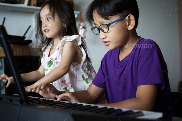 Brother and little sister are playing keyboard instrument together ...