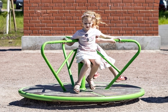 The toddler girls are riding a carousel on the playground. Sisters ...