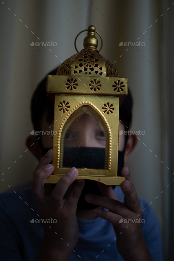 islamic design gold lantern with young boy wearing face mask looking ...