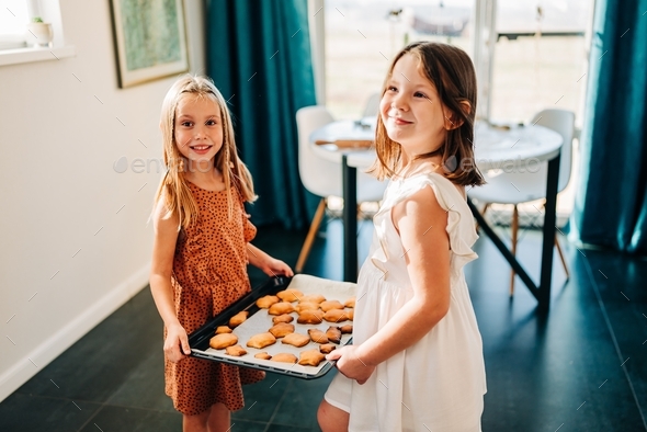 Kids girls cooked cookies and bringing them to the table on the kitchen ...
