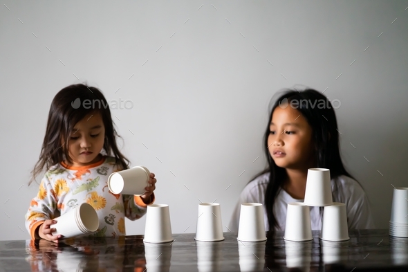 children playing paper cups stacking game at home. young girls siblings ...
