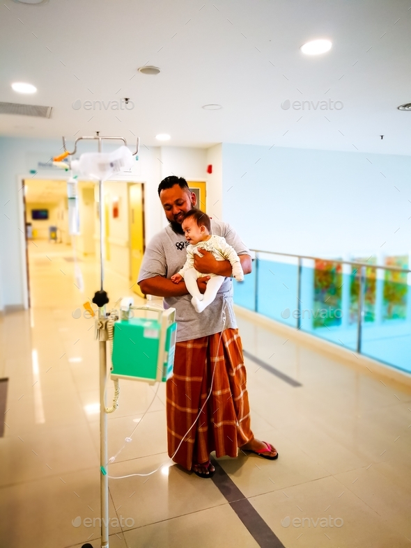 Baby and father attached to the iv drip machine is walking together in ...