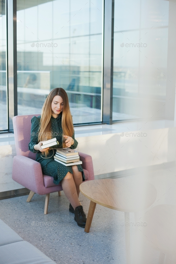 Woman in public library with a stack of books, smiling and sitting in ...