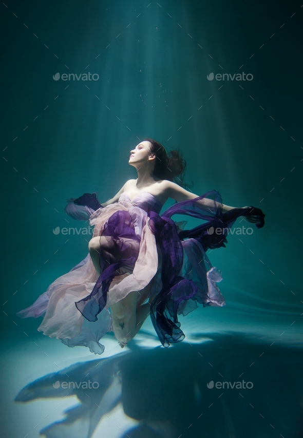Beautiful woman wearing purple dress freediving in the pool of ...