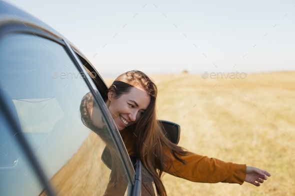 Happy woman with long hair traveling on a road trip looking out of the ...