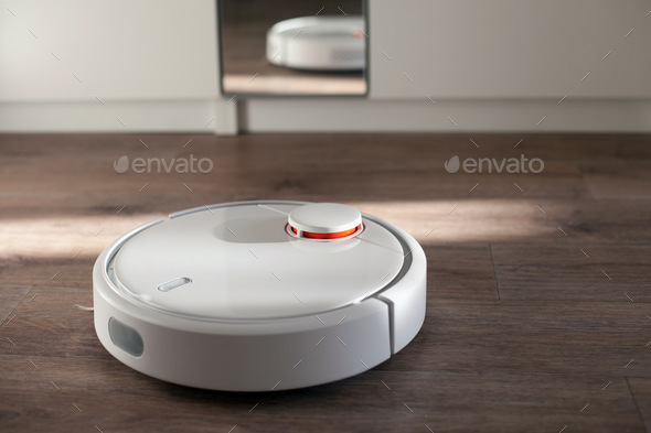 A white robotic vacuum cleaner removing dust from the floor, technology ...