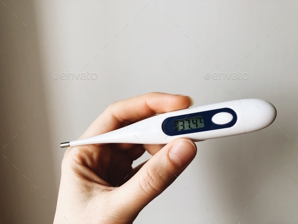 Hand holding digital thermometer to measure body temperature showing ...
