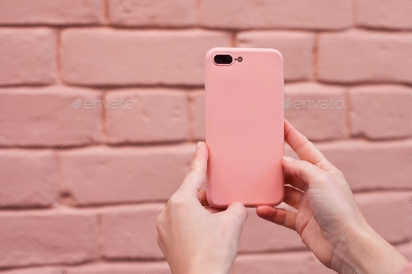 Woman holding pink mobile phone on a pink brick wall background Stock ...