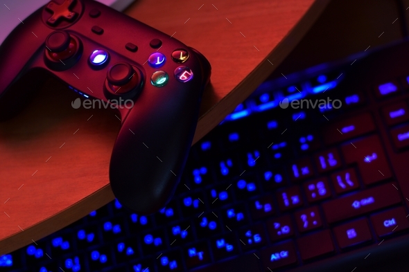 Modern gamepad lies with pc keyboard on table in dark playroom scene ...