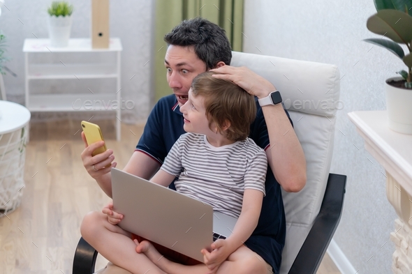 Surprised young man sit on computer using laptop relax with preschooler ...