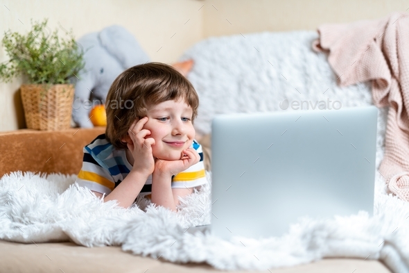 Child kid boy using laptop. Watching movie. Lying on couch at home ...