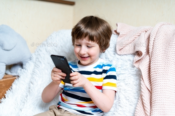 Child kid boy texting at mobile phone at home. Having , video chat and ...