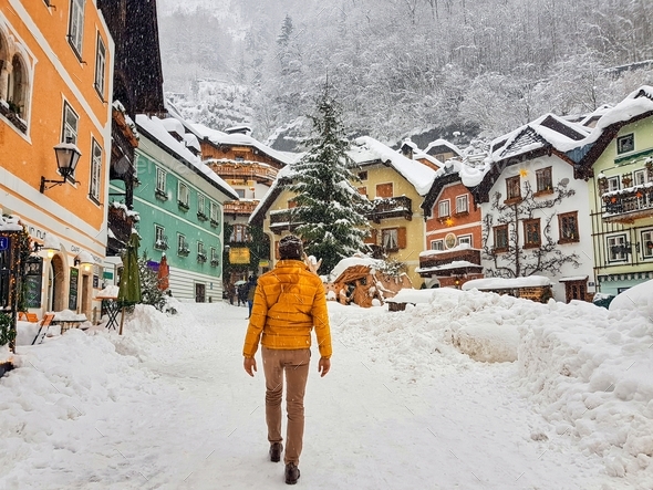 Rear view of man in yellow winter jacket in snow covered town ...