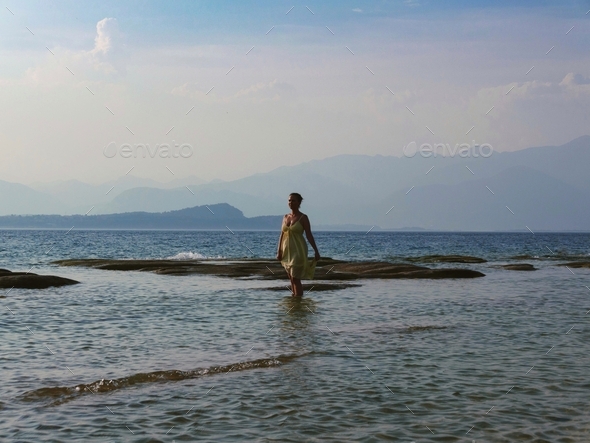 Full length portrait of young girl walking in ankle deep water on beach ...