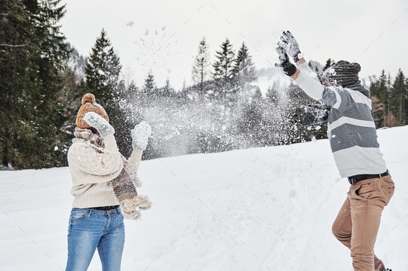 Young couple wearing winter sweaters having a snowball fight outdoors ...