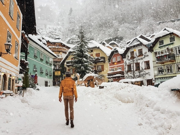 Rear view of man in yellow winter jacket in idyllic snow covered town ...