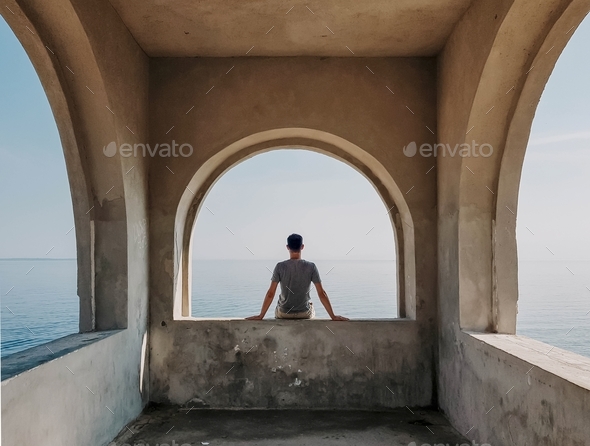 Rear view of man sitting in arched window overlooking sea Stock Photo ...