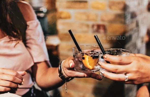 Close-up image of women holding cocktails and clinking glasses on night ...