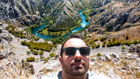 Young man taking a selfie with amazing panorama of river canyon in ...