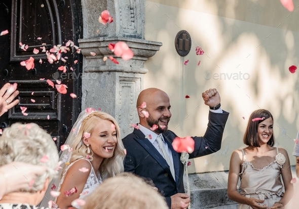 Bride and groom coming out of church, wedding guests throwing flower ...
