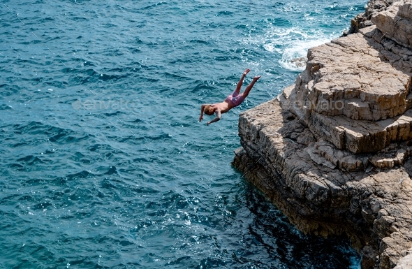 Man in mid-air jumping from cliff into the ocean Stock Photo by 9_fingers_