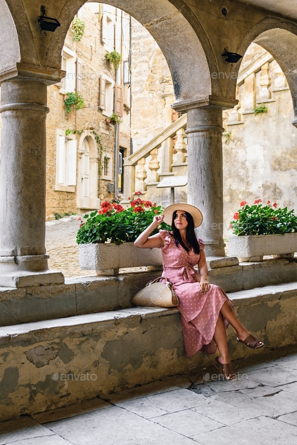 Gorgeous young woman sitting under arches of an old building, town ...