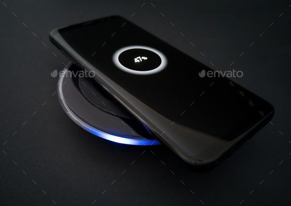 Close-up image of black mobile phone charging on wireless charger ...