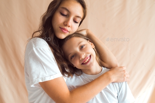 sisters hugging on beige color textile background Stock Photo by shapoval08