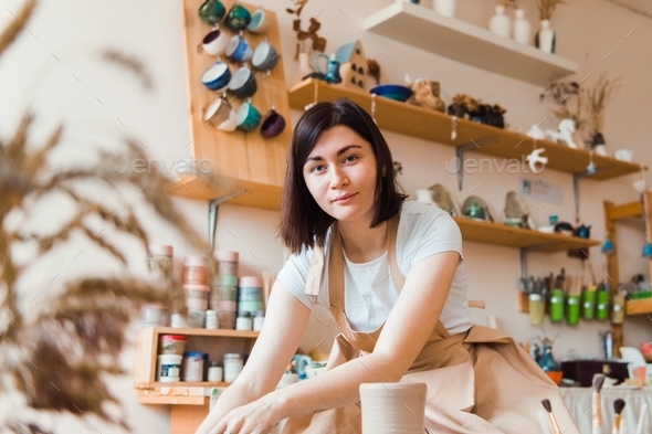 Beautiful brunette girl making clay pot in pottery workshop. Look at ...