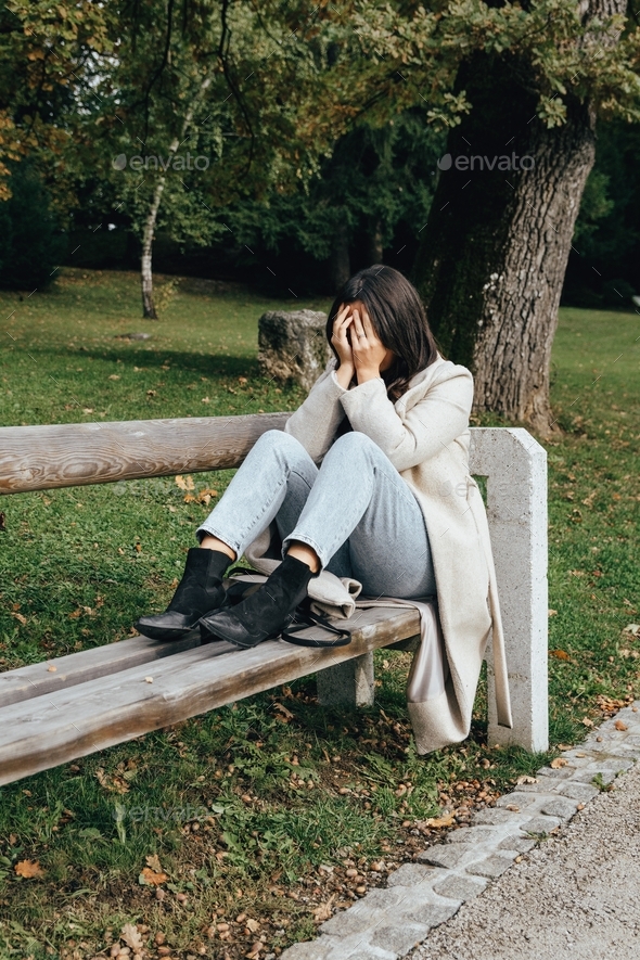 Sad and depressed Young woman sitting on bench in park, holding head in ...