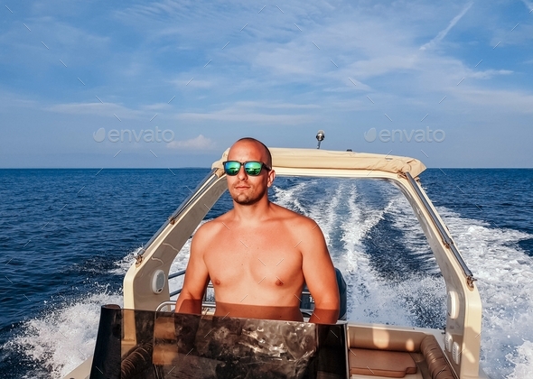 Portrait of fit shirtless young man piloting a boat. Sea, summer ...
