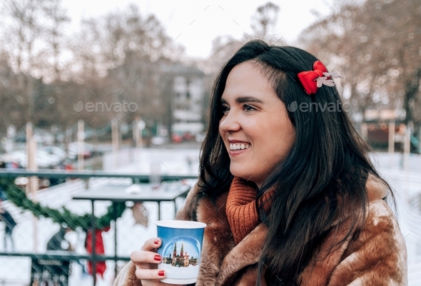 Portrait of happy beautiful young woman holding cup of mulled wine at ...